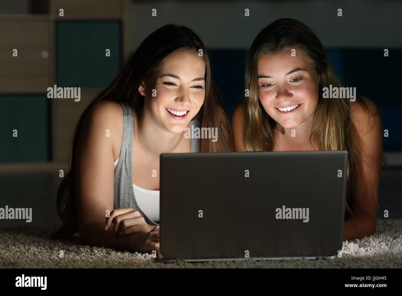 Two teens watching on line content in a laptop lying on the floor in a ...