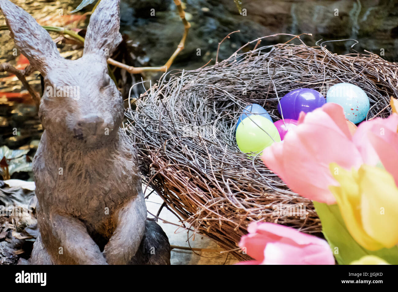 A stone Easter bunny sitting beside a nest of colored eggs Stock Photo ...