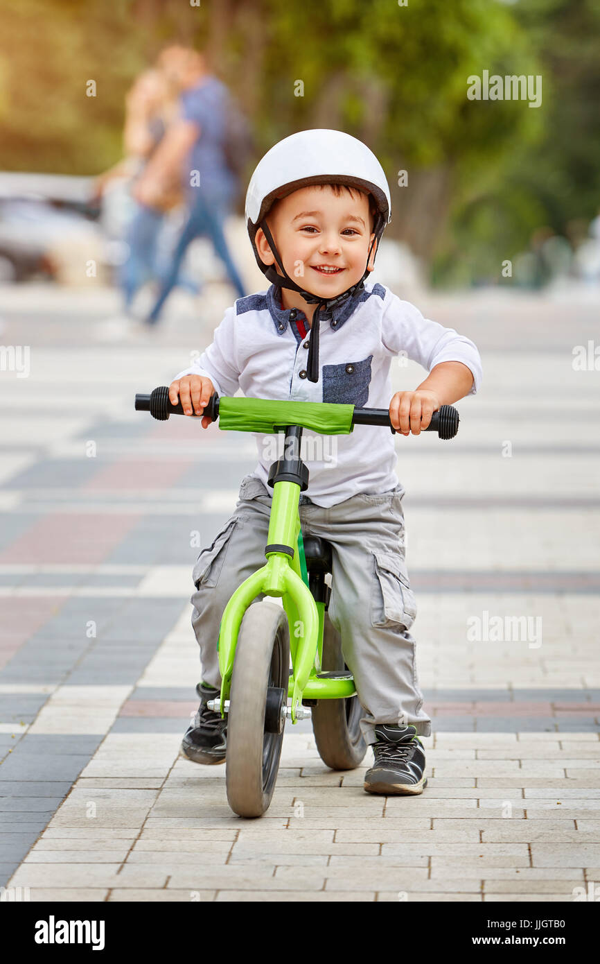 Happy boy in white helmet ride his first bike in city park Stock Photo ...