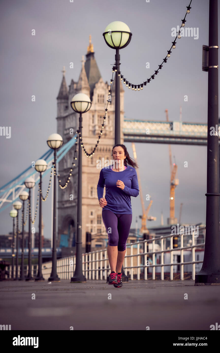A woman running alongside the River Thames with Tower Bridge in the ...