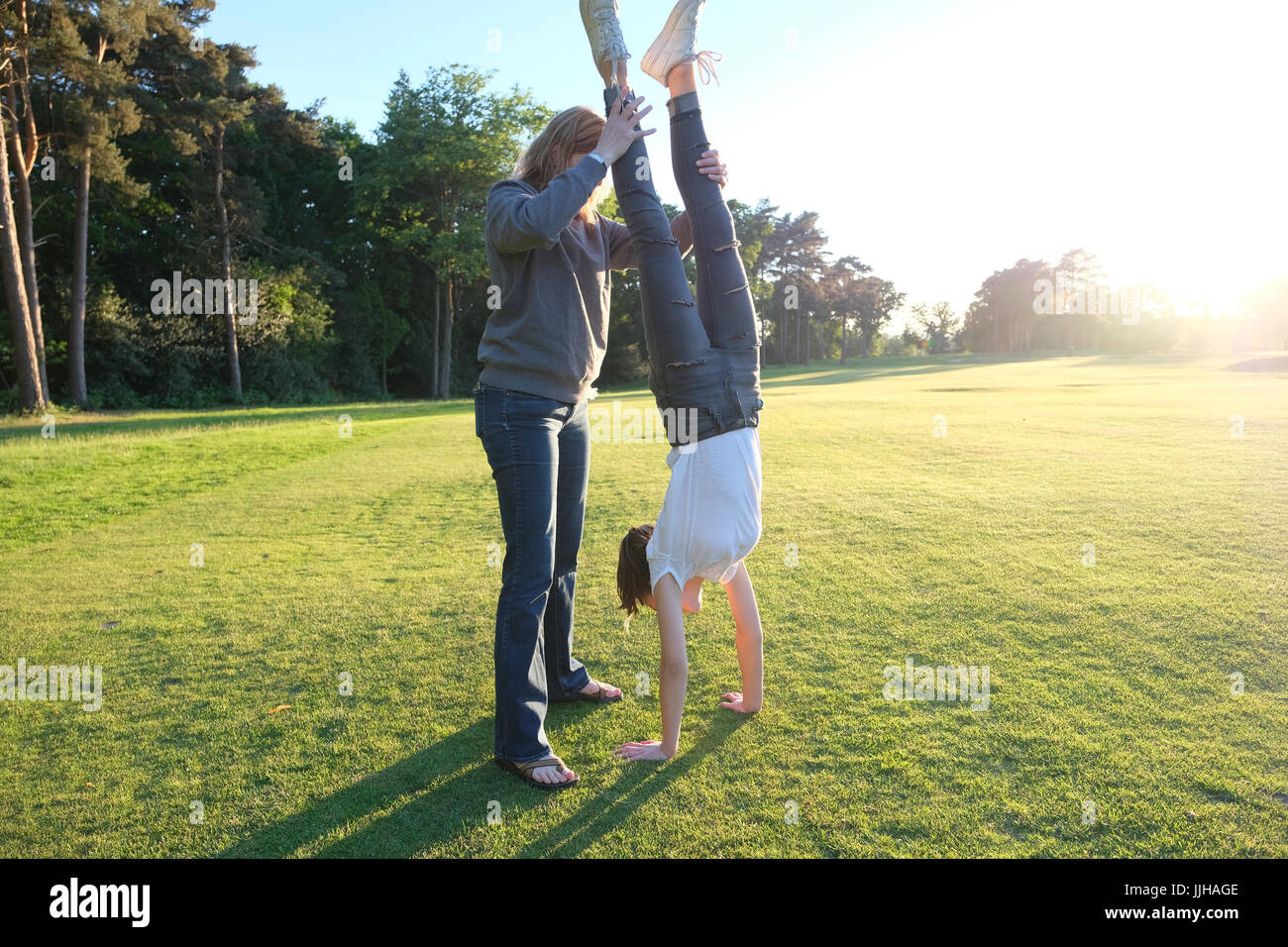 A woman helping her daughter with a handstand on a sunlit day Stock ...