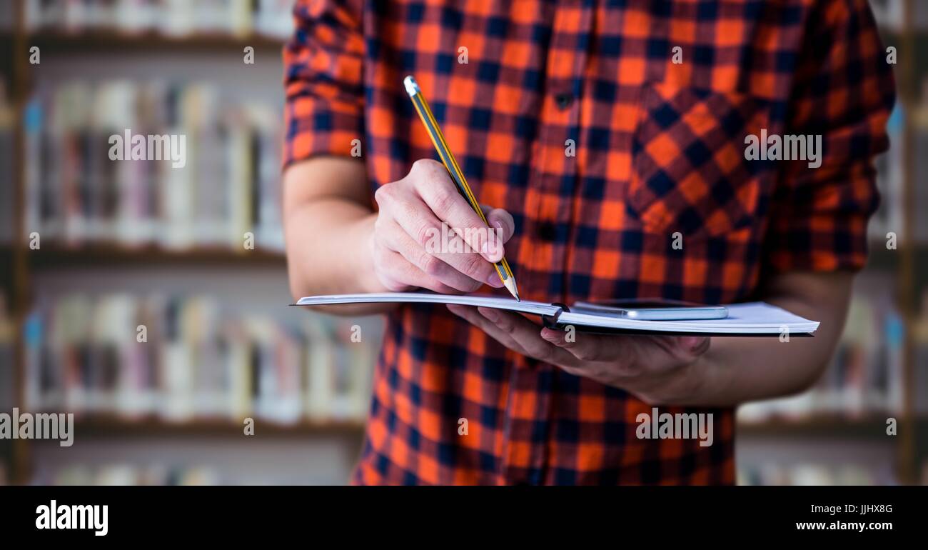 College student mid section with notebook against blurry bookshelf ...