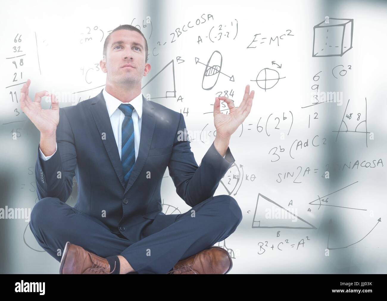 Business man meditating in blurry grey office with flare and math ...