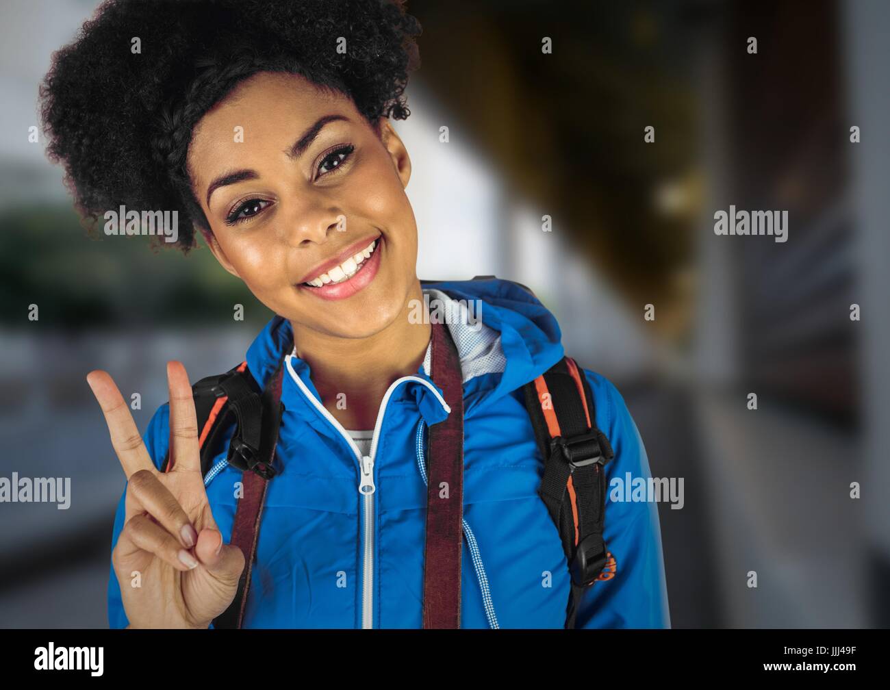 Millennial backpacker making peace sign against blurry train station ...