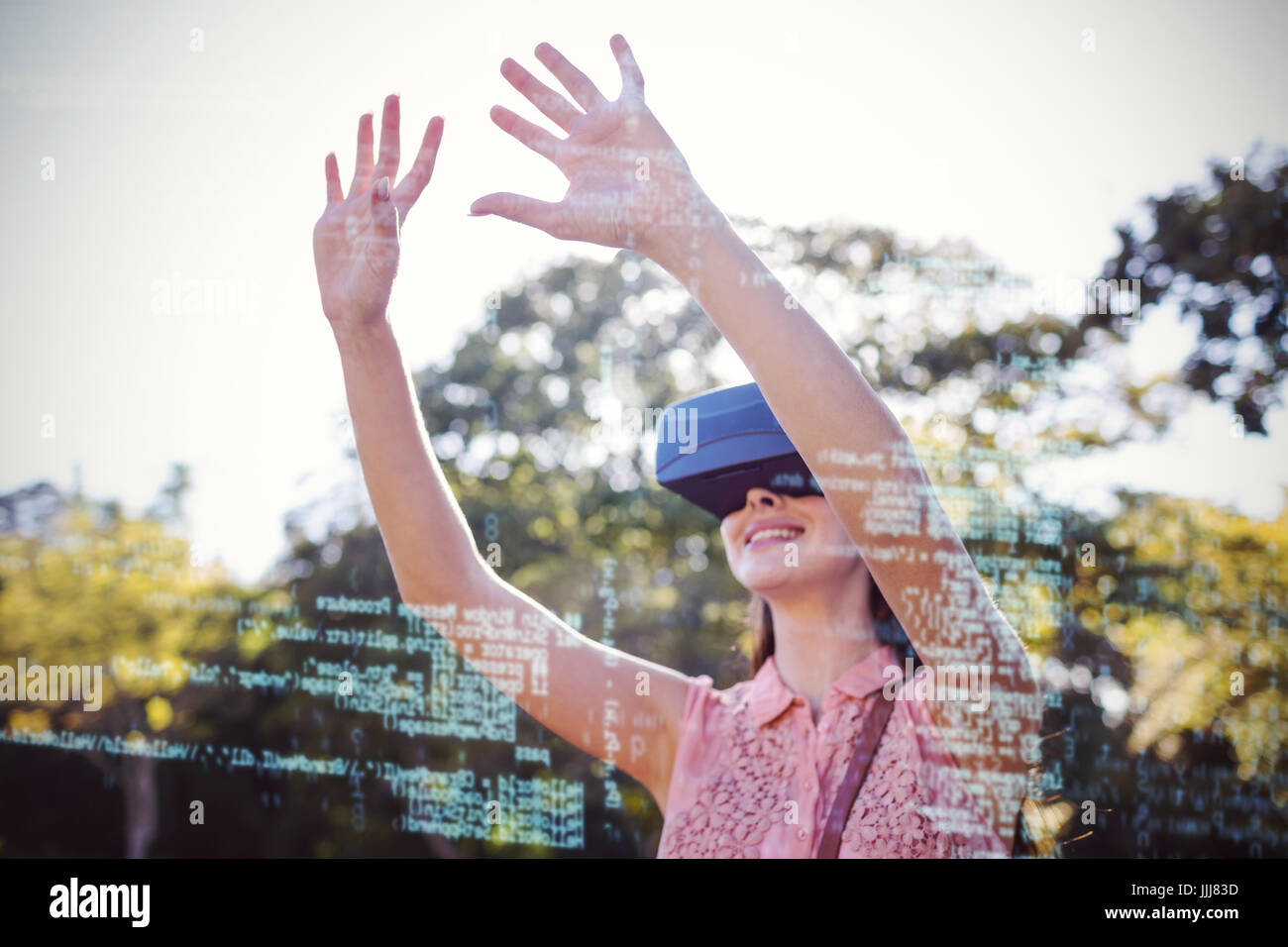 Smiling woman raising her hands while using a VR 3d headset in the park ...