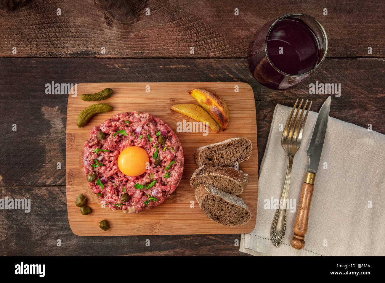 A photo of a steak tartare with a raw egg yolk, gherkins, capers, rye ...