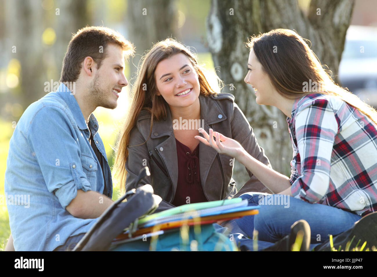 Three students talking after classes beside books and ruckpacks sitting ...