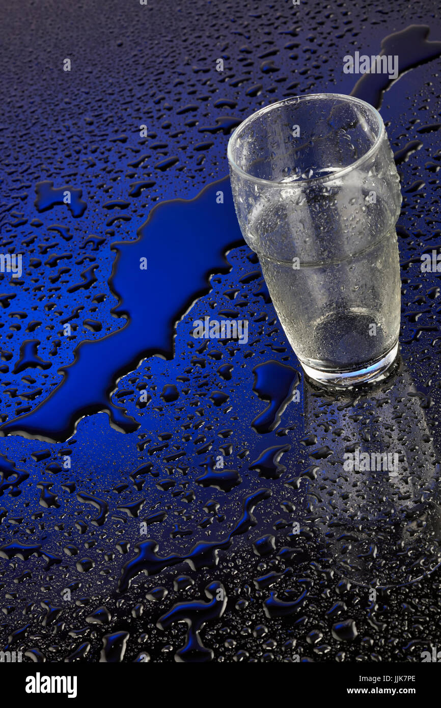 Glass of water spilled with drops on light background Stock Photo - Alamy