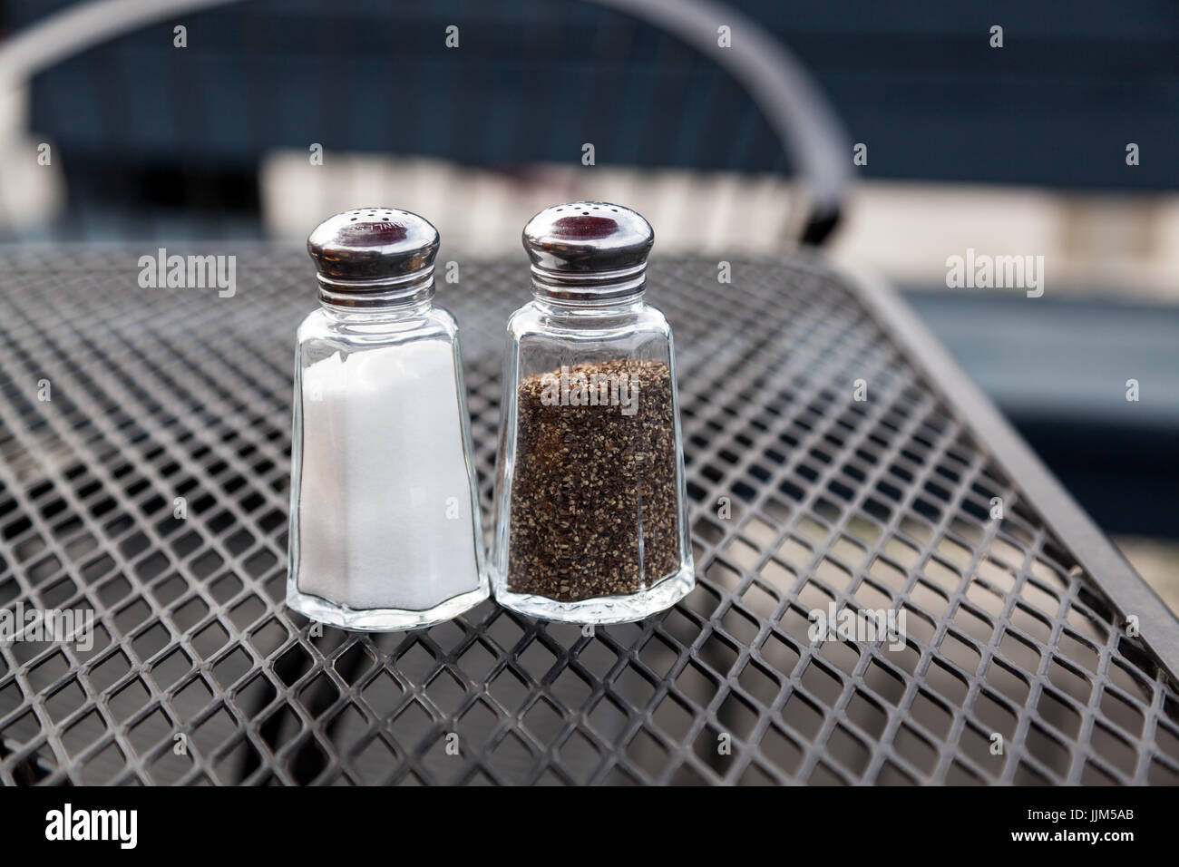 Classic glass salt and pepper shakers on a metal grate table at a patio ...