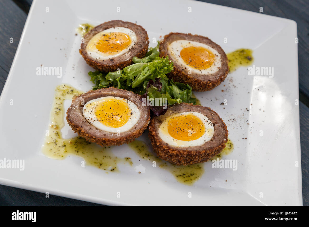 Artisan eggs in sausage shells on a white plate with garnish on a patio ...