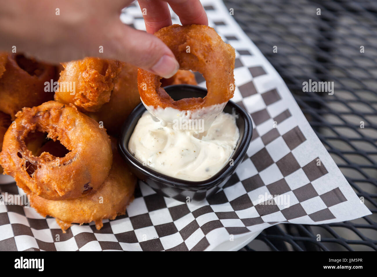 A hand dipping a large deep fried beer battered onion ring into a ...