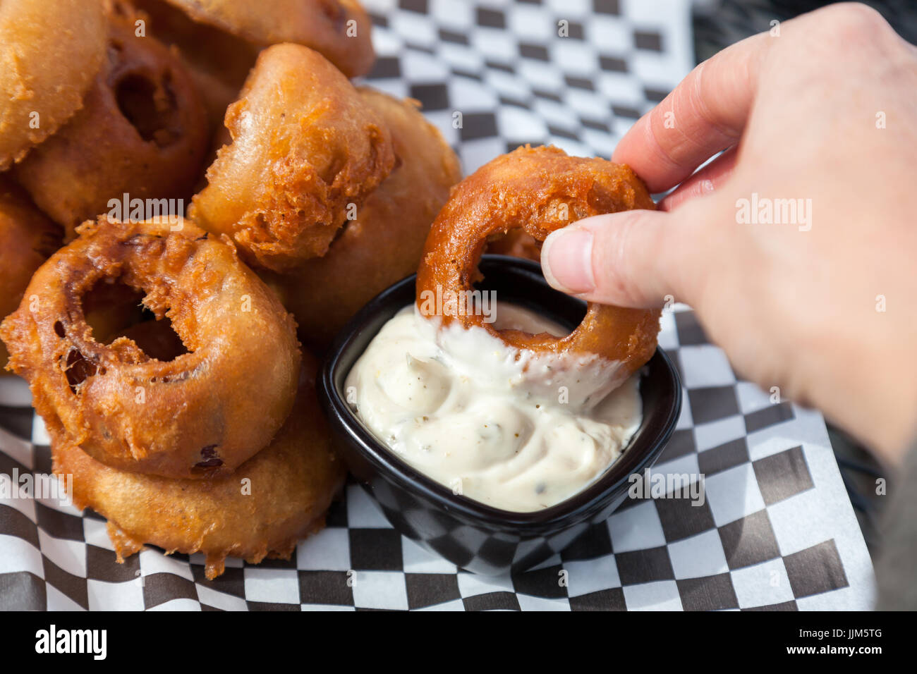 A hand dipping a large deep fried beer battered onion ring into a ...
