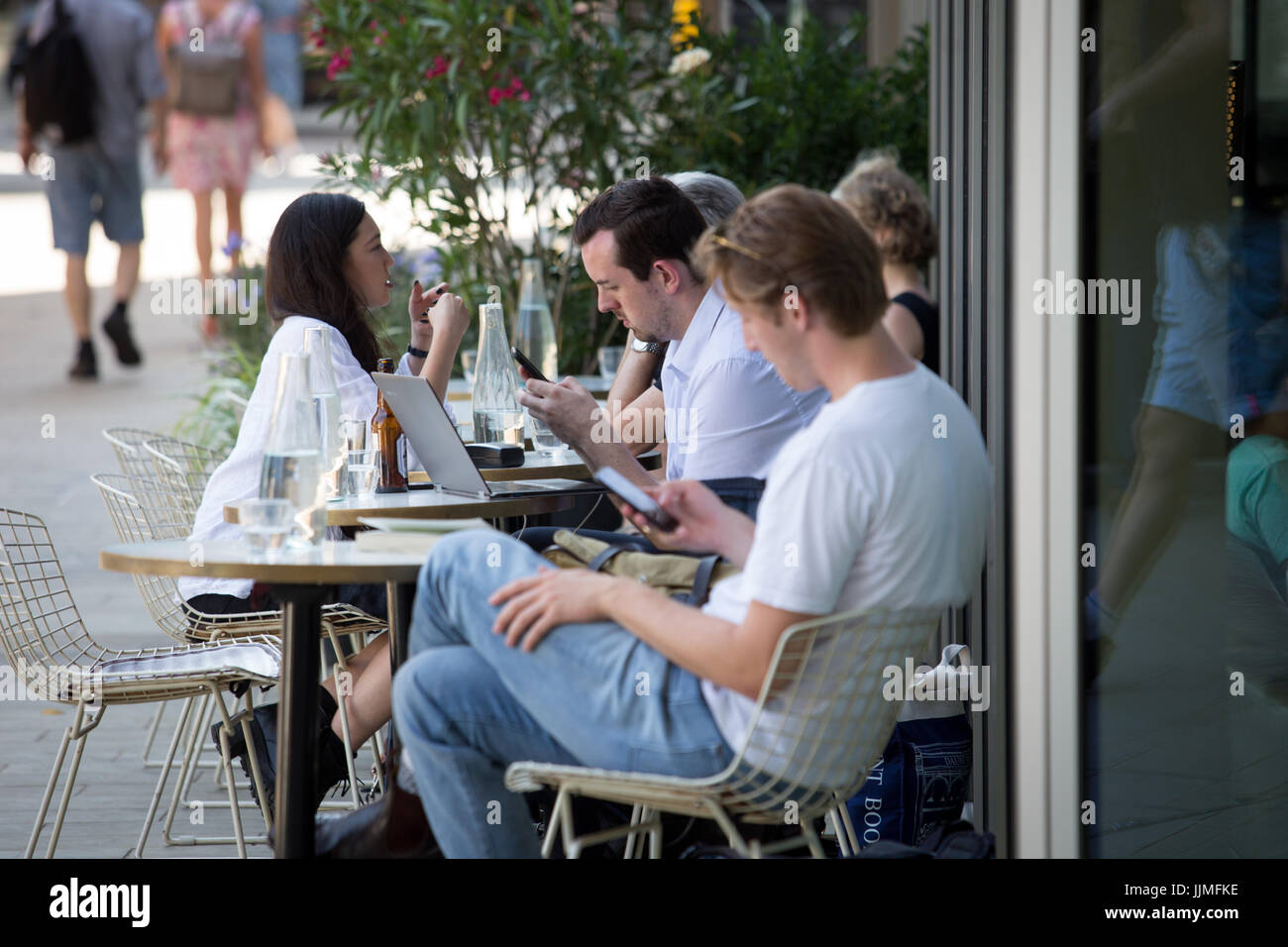 People sitting outside a cafe talking, using phones and laptops. Taken ...