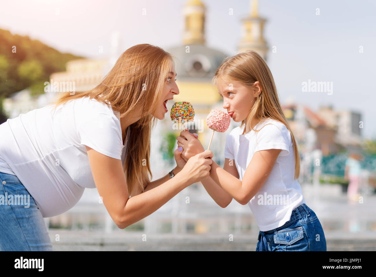 Cute little girl and her pregnant mother eating candy apples at fair in ...