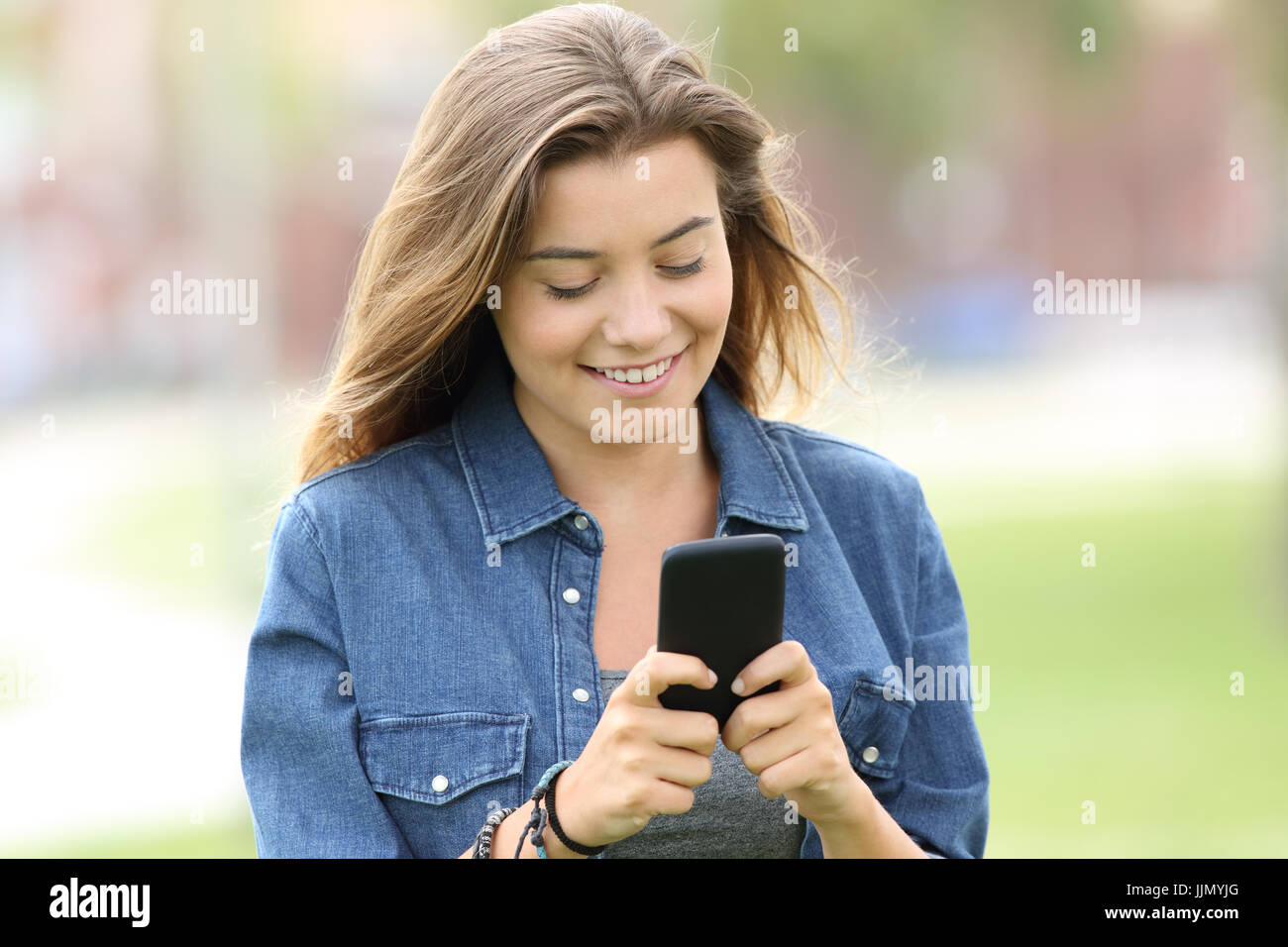 Portrait of a happy teen walking and reading text in a smart phone in ...