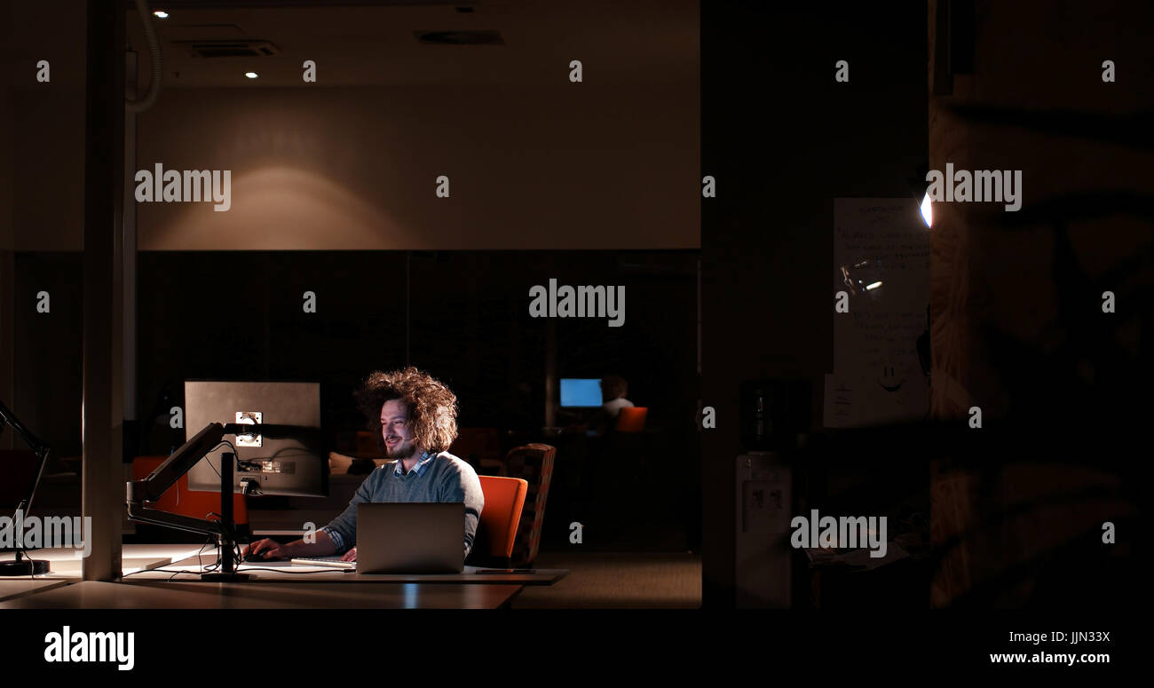 Young man working on computer at night in dark office. The designer ...