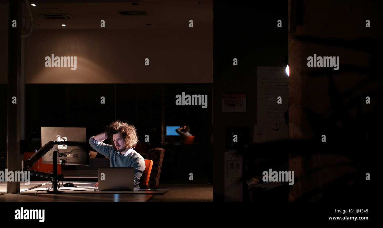 Young man working on computer at night in dark office. The designer ...