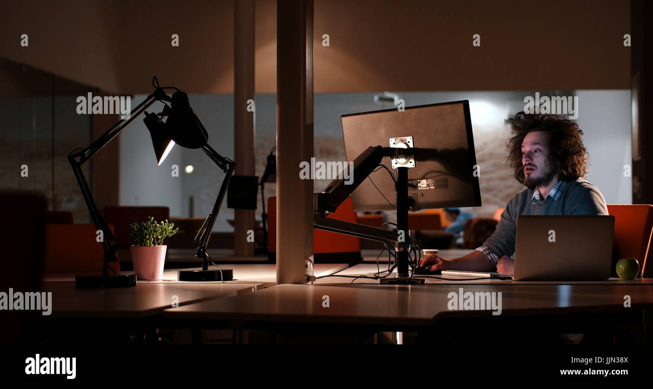 Young man working on computer at night in dark office. The designer ...