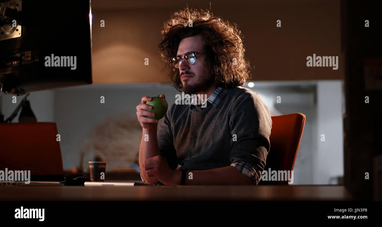 Young man working on computer at night in dark office. The designer ...