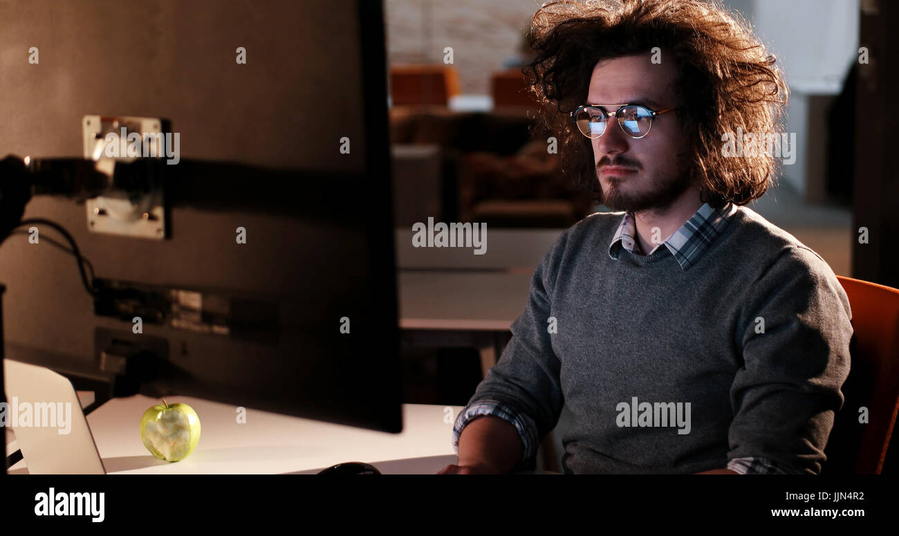 Young man working on computer at night in dark office. The designer ...