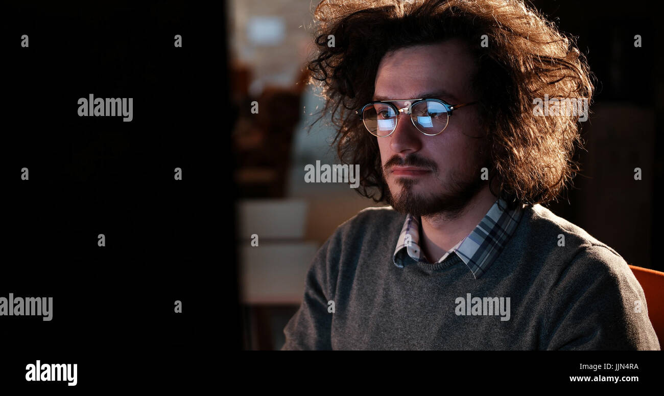 Young man working on computer at night in dark office. The designer ...