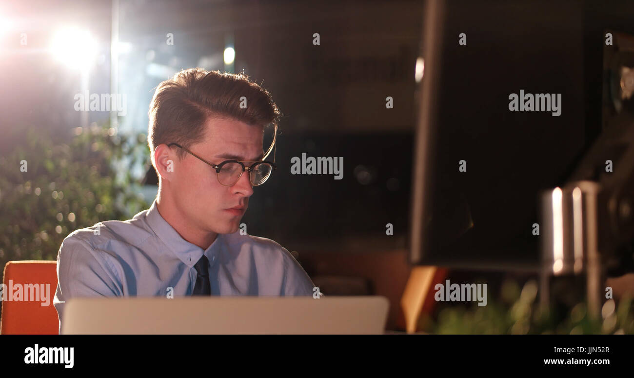 Young man working on computer at night in dark office. The designer ...