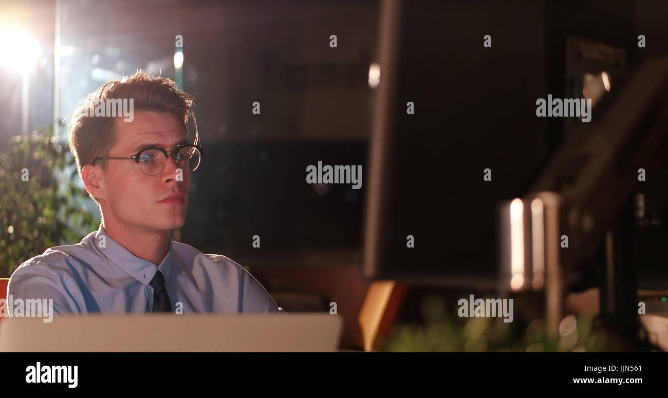 Young man working on computer at night in dark office. The designer ...