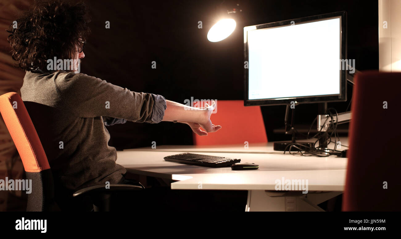 Young man working on computer at night in dark office. The designer ...