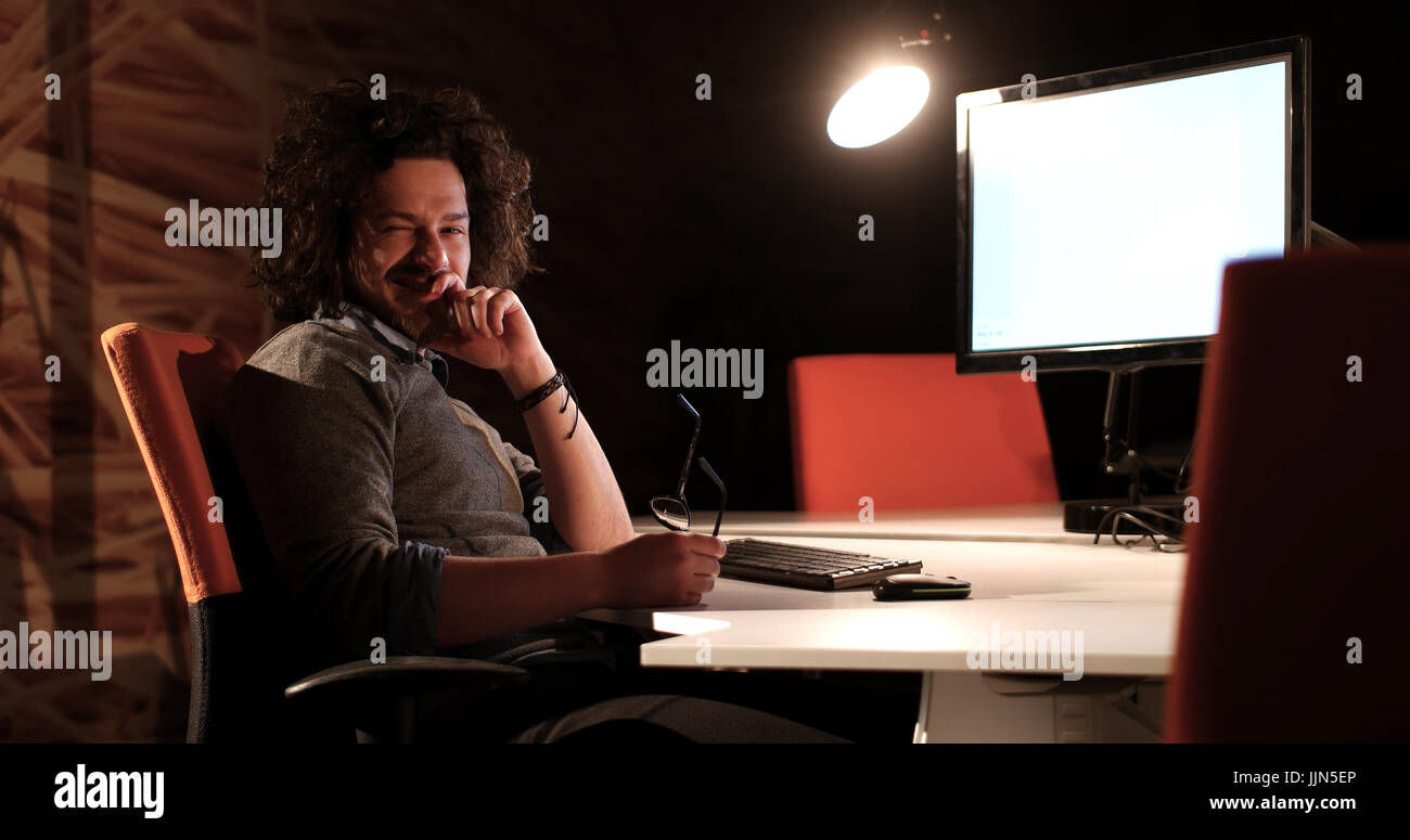 Young man working on computer at night in dark office. The designer ...