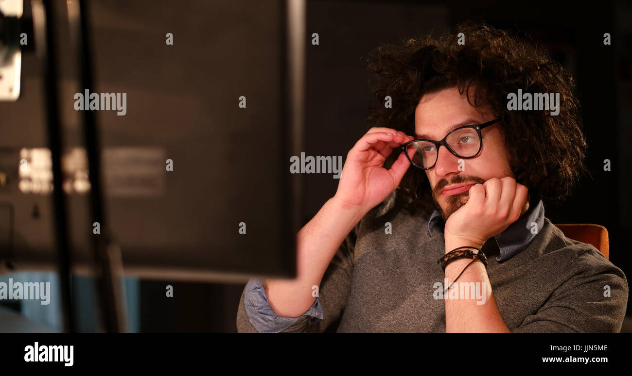 Young man working on computer at night in dark office. The designer ...