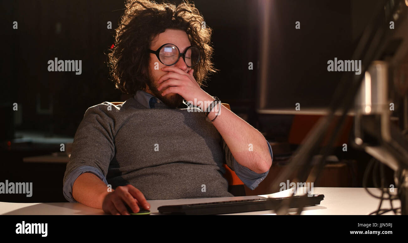 Young man working on computer at night in dark office. The designer ...