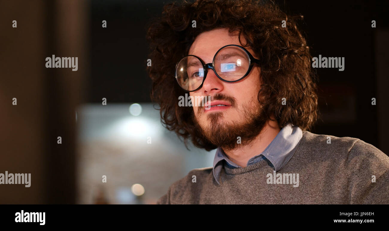 Young man working on computer at night in dark office. The designer ...