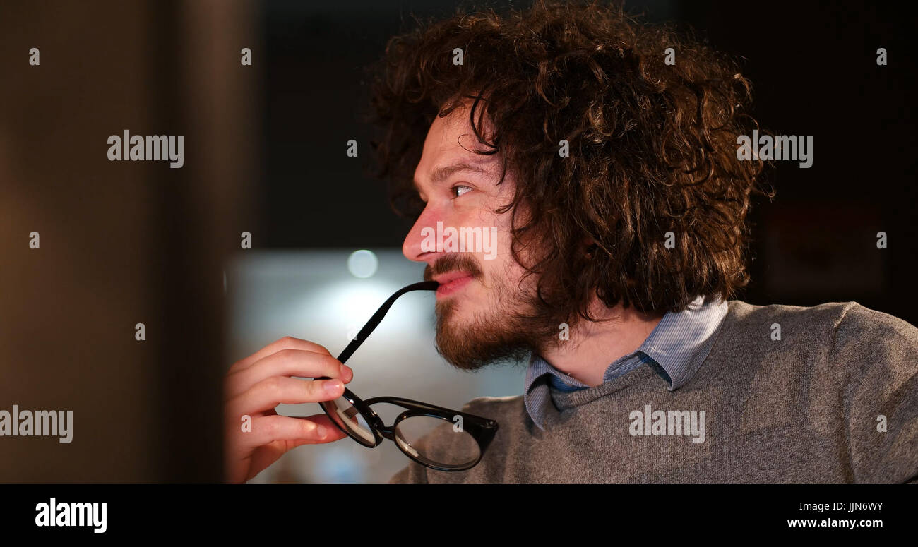Young man working on computer at night in dark office. The designer ...