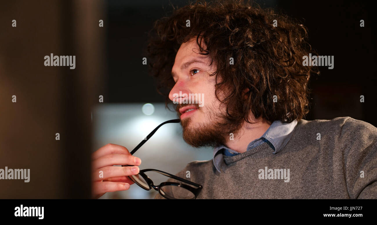 Young man working on computer at night in dark office. The designer ...