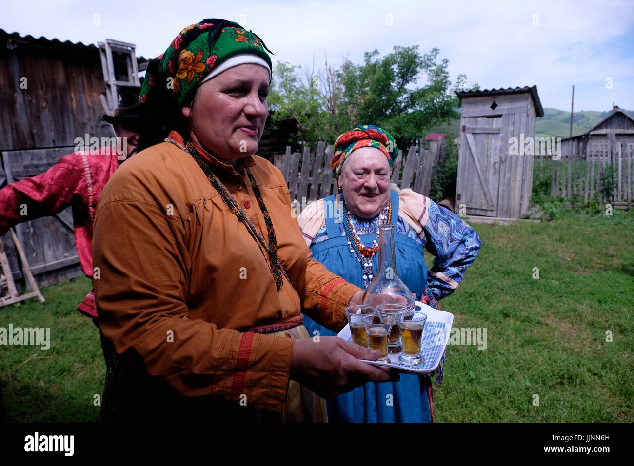 Russian women wearing traditional sarafan dress serve homemade Samogon ...