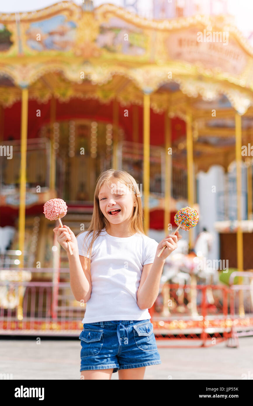 Cute little girl eating candy apple and posing at fair in amusement ...