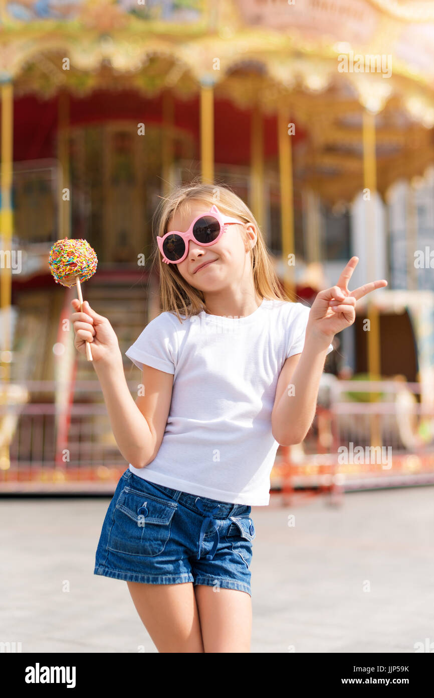 Cute little girl eating candy apple and posing at fair in amusement ...