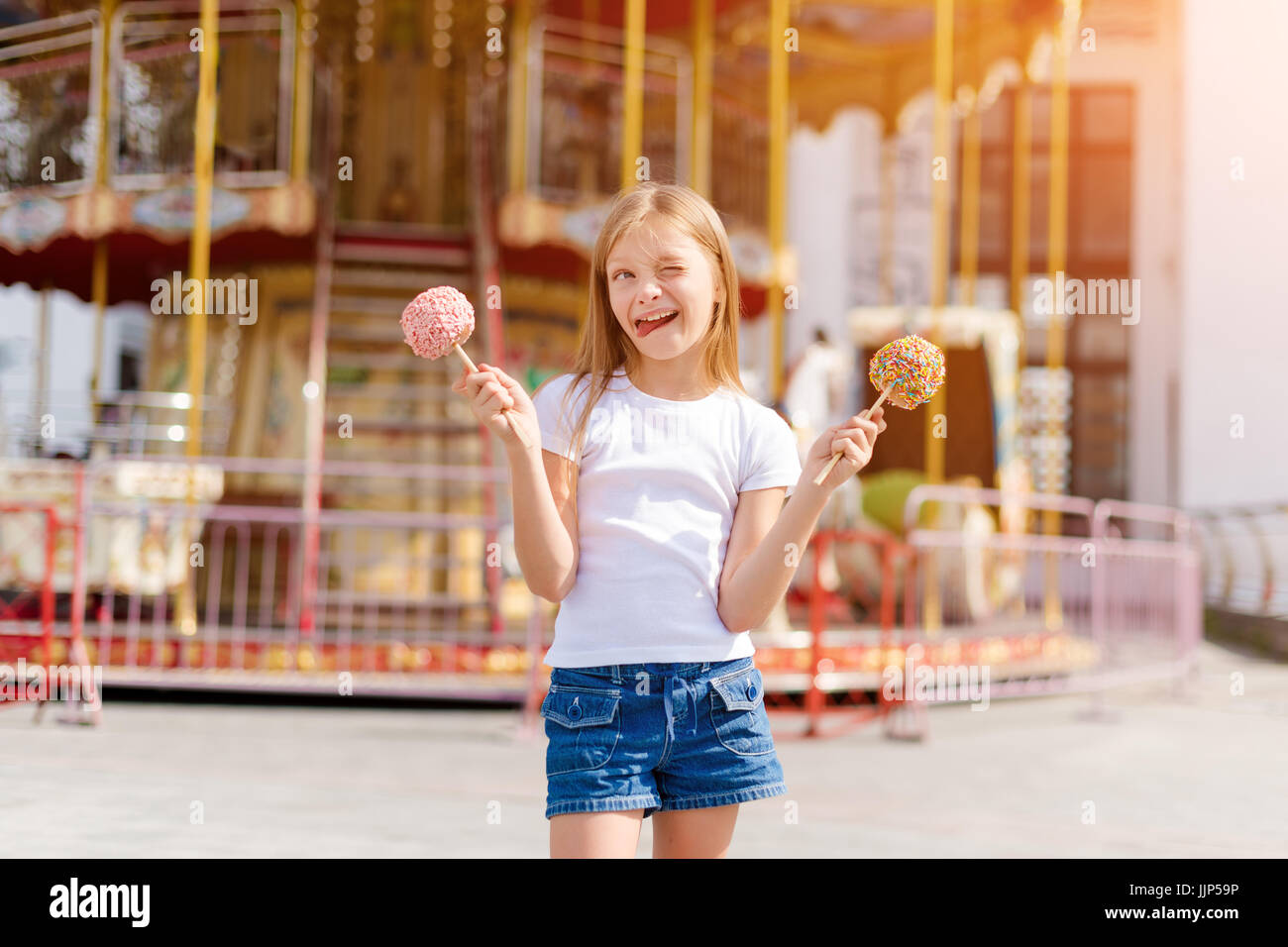 Cute little girl eating candy apple and posing at fair in amusement ...