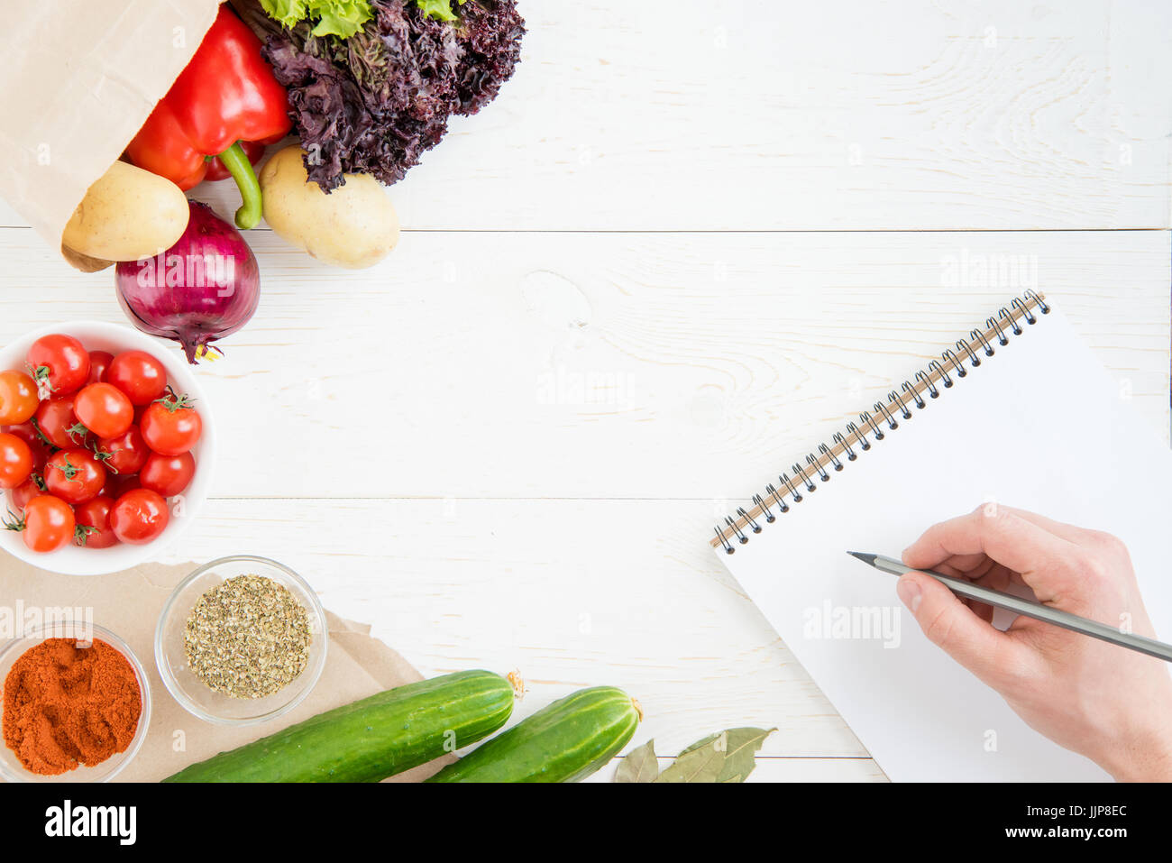 Close-up partial view of person holding pencil and writing recipe in ...