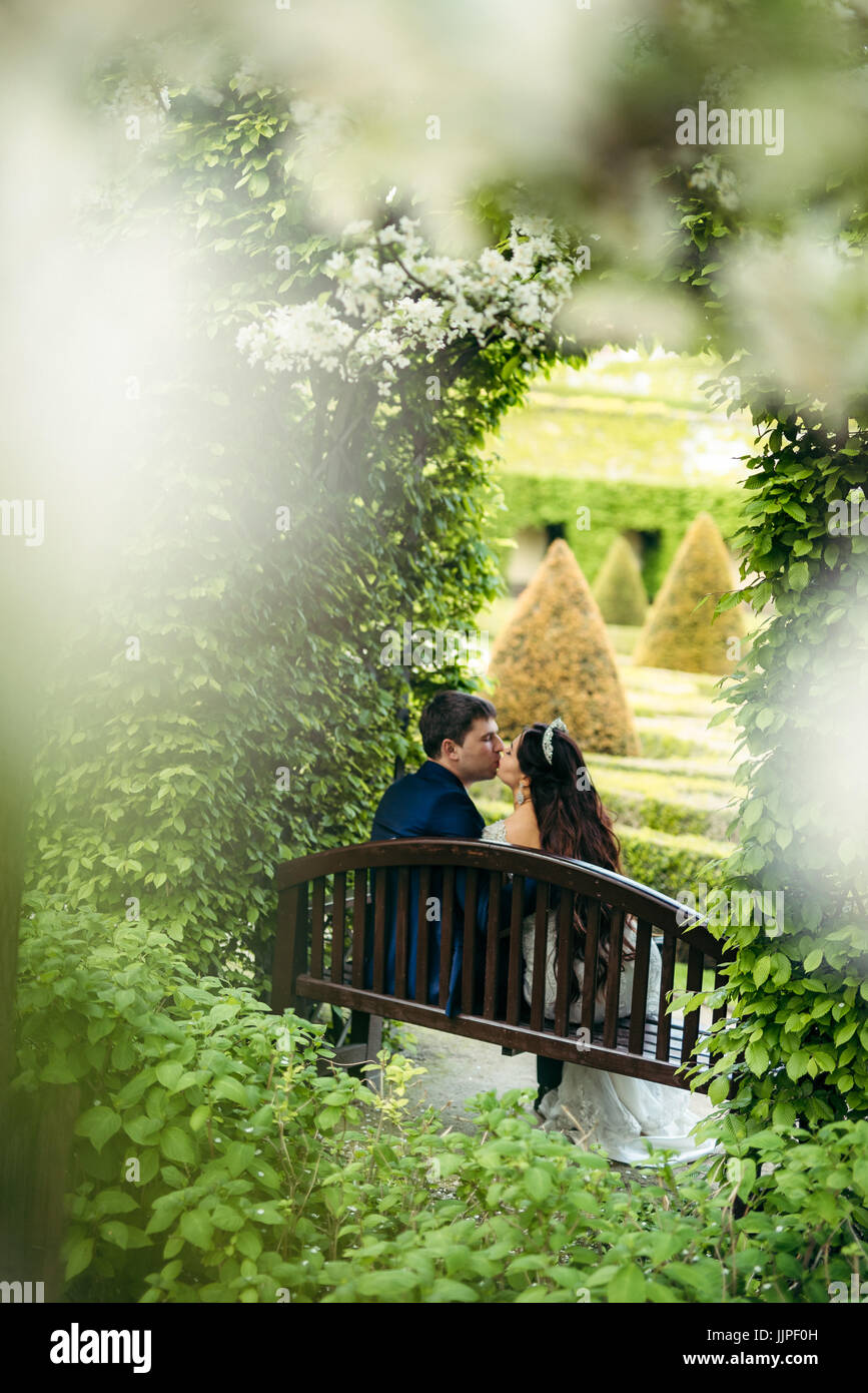 Back view of the beautiful kissing newlywed couple sitting on the bench ...
