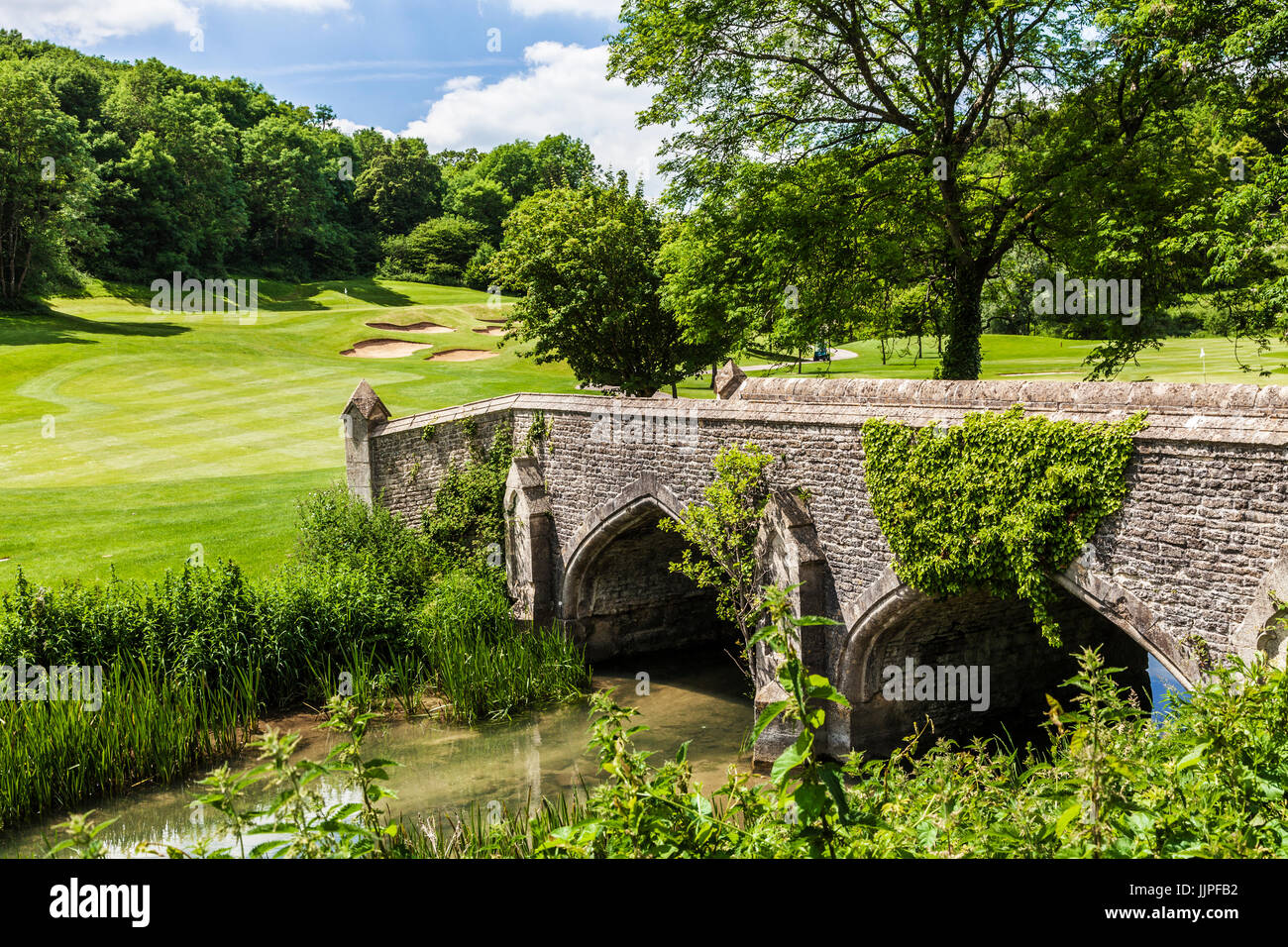 A stone footbridge over the River Bybrook with a golf course beyond ...