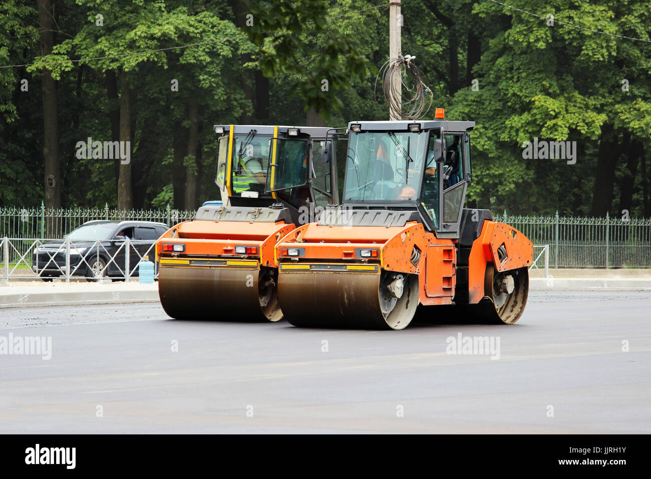 Two orange compactors make asphalt in the future parking lot for ...
