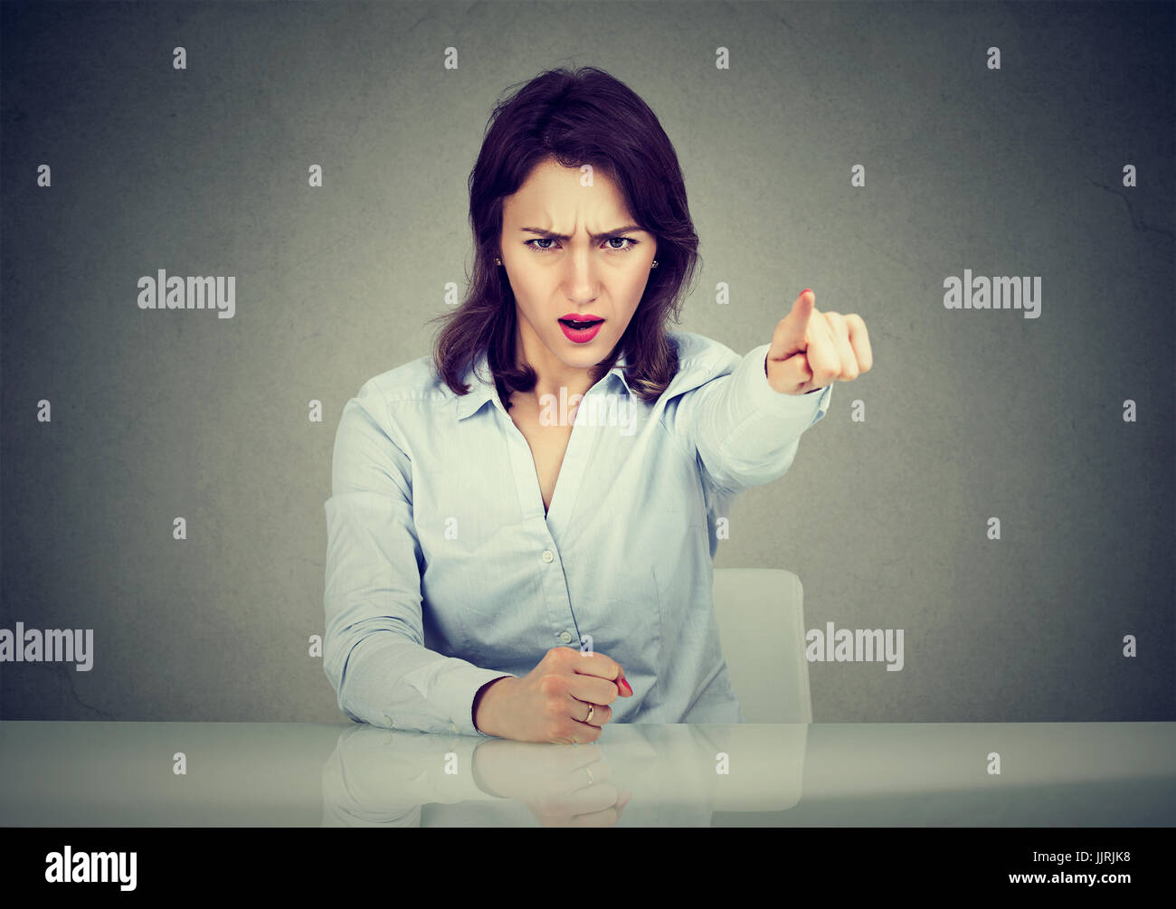 Angry business woman sitting at her desk and screaming pointing with ...