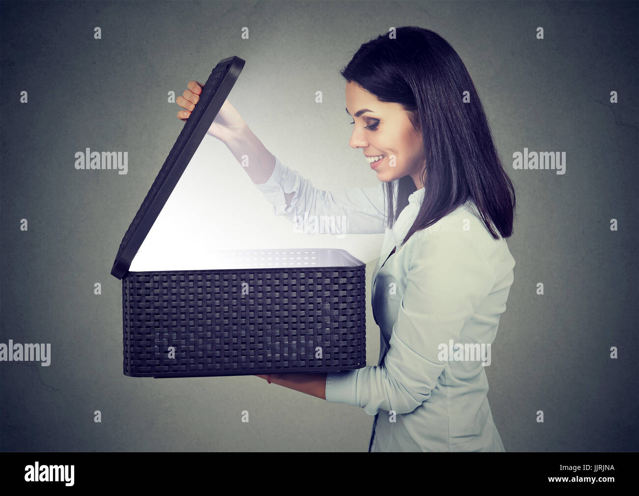 Happy woman opening looking into gift box with bright light coming out ...