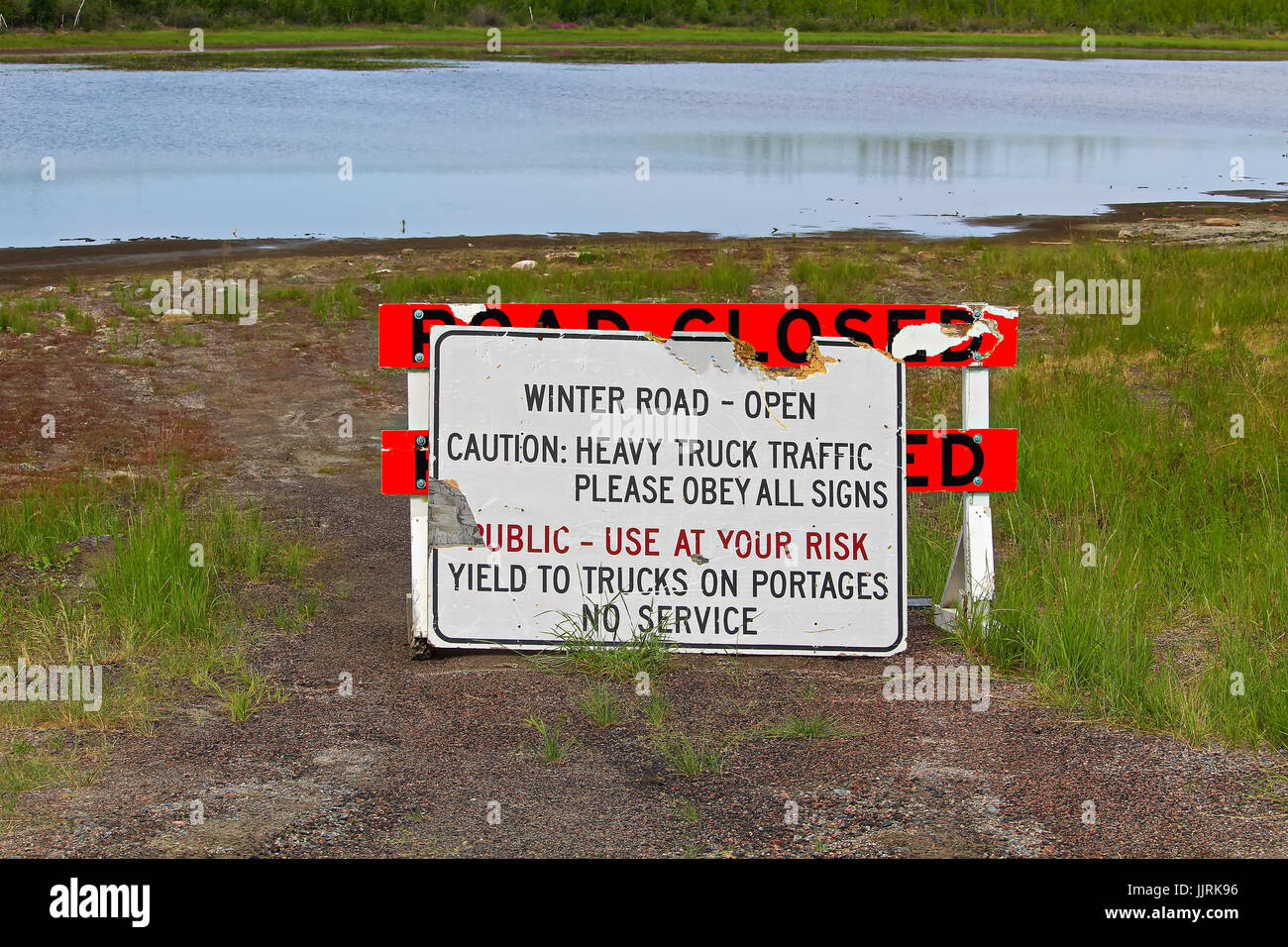 A road closed barricade and a winter road open sign leaning against ...