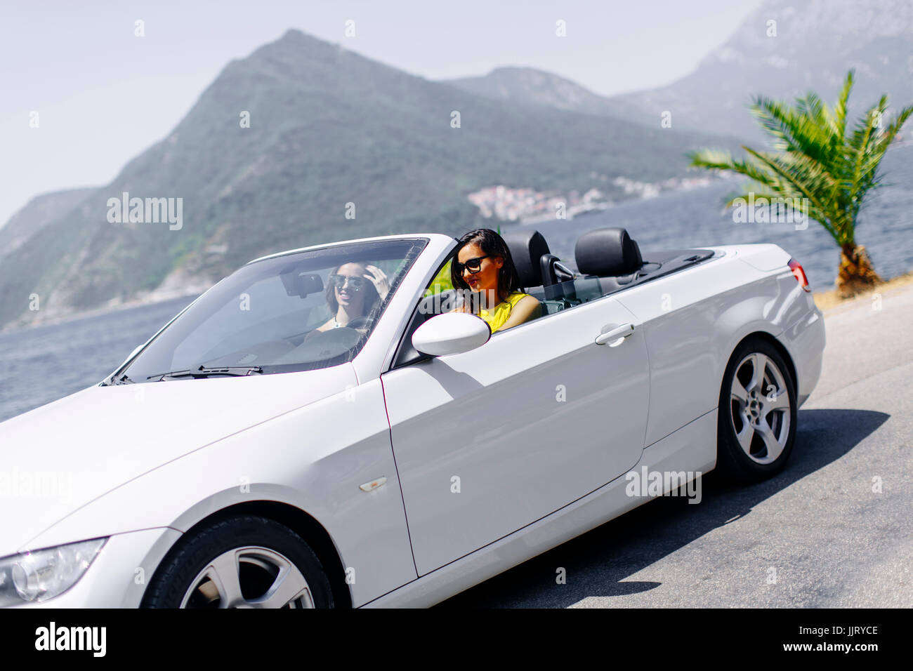 Two happy friends in white cabriolet car driving everywhere and looking ...