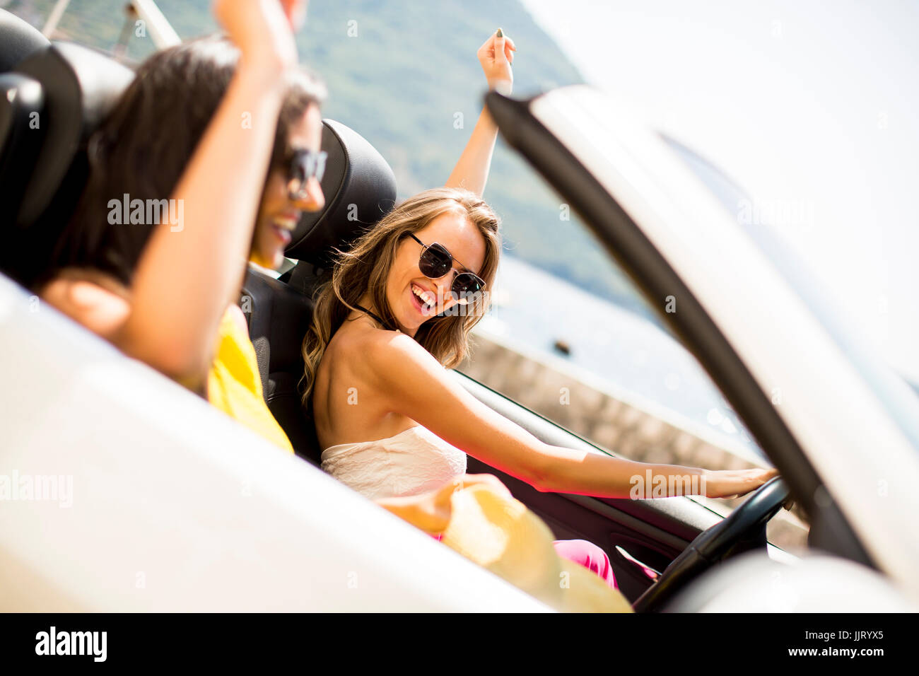 Two happy friends in white cabriolet car driving everywhere and looking ...