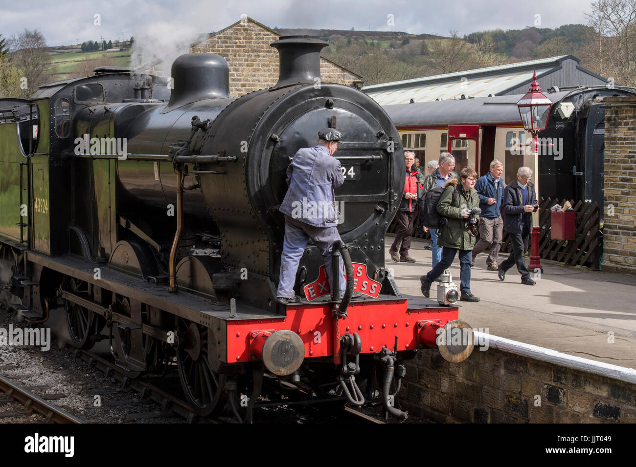 People on platform walk past train driver climbing on front of steam ...