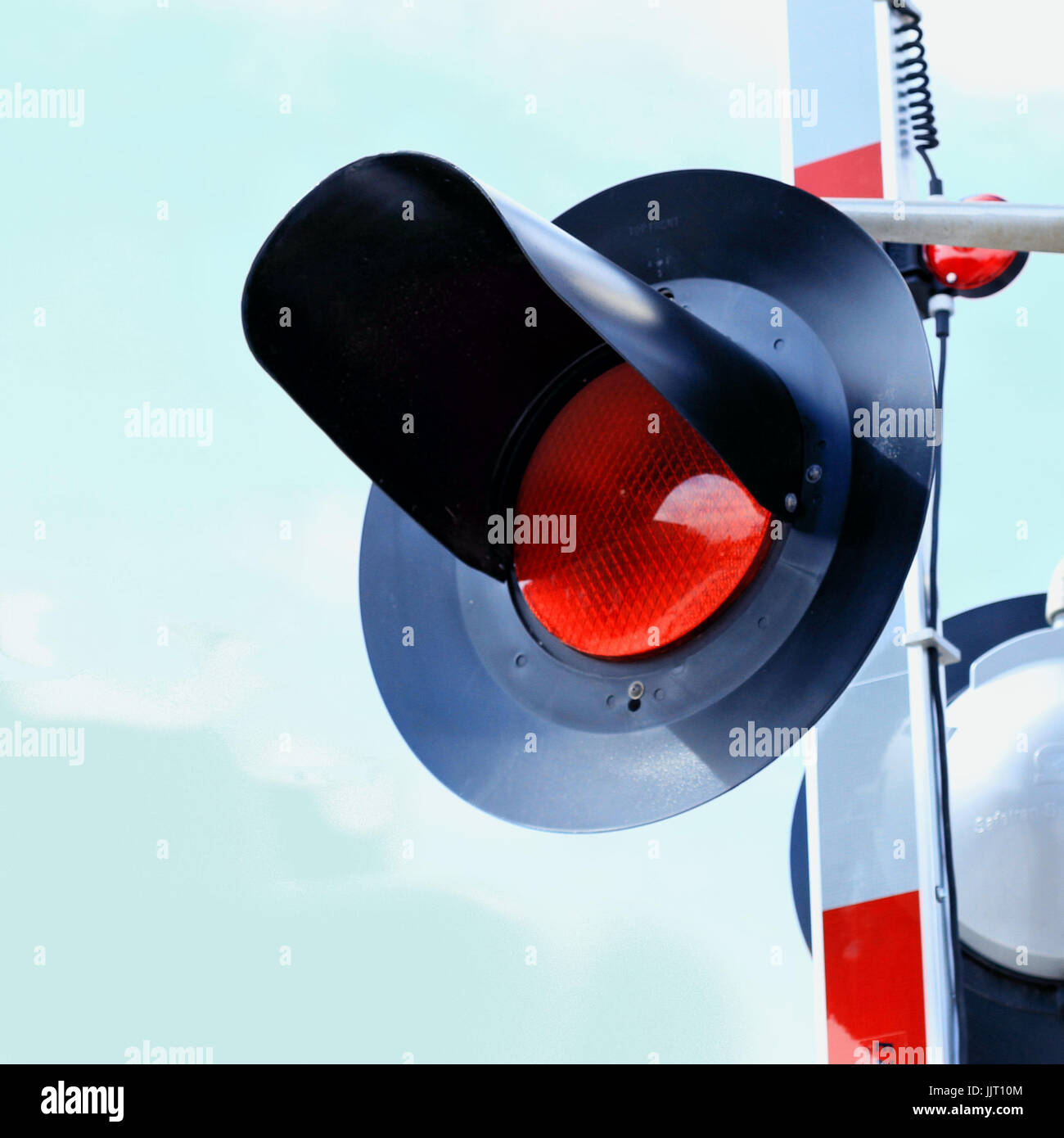 A railroad crossing light and arm stand at attention against a blue sky ...