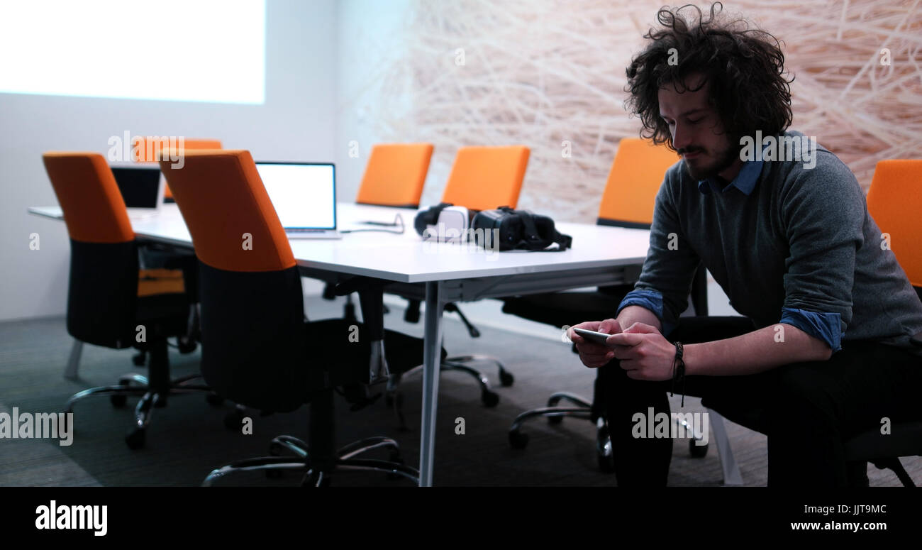 Young man using mobile phone while working on computer at night in dark ...